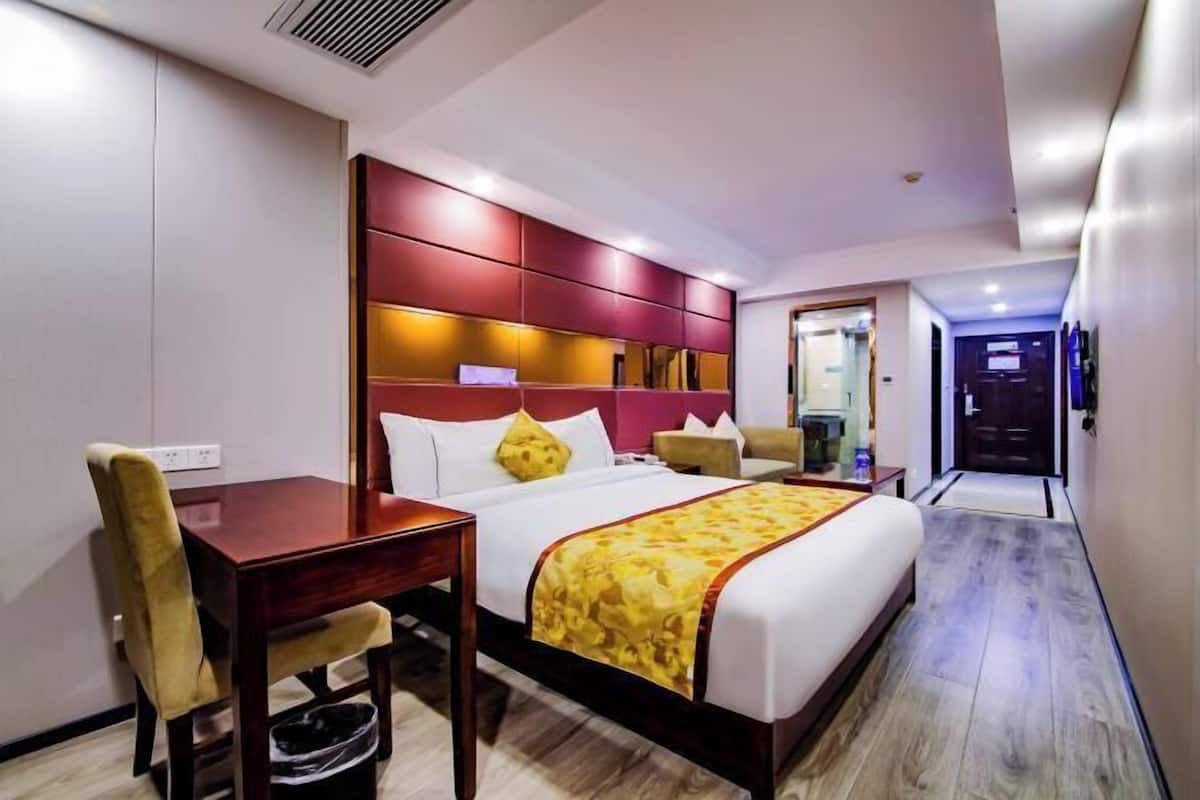 Quarto de hotel com cama, mesa de cabeceira, cadeira e escrivaninha.
