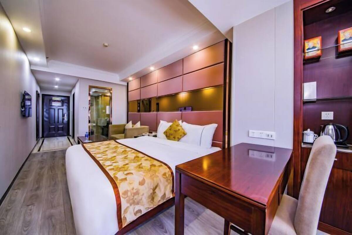 Quarto de hotel com uma cama grande, uma escrivaninha de madeira, uma cadeira e uma estante embutida com obras de arte.