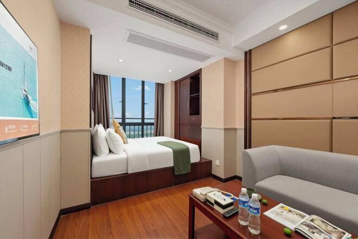 Quarto de hotel com cama, sofá, mesa com objetos e janela com vista.