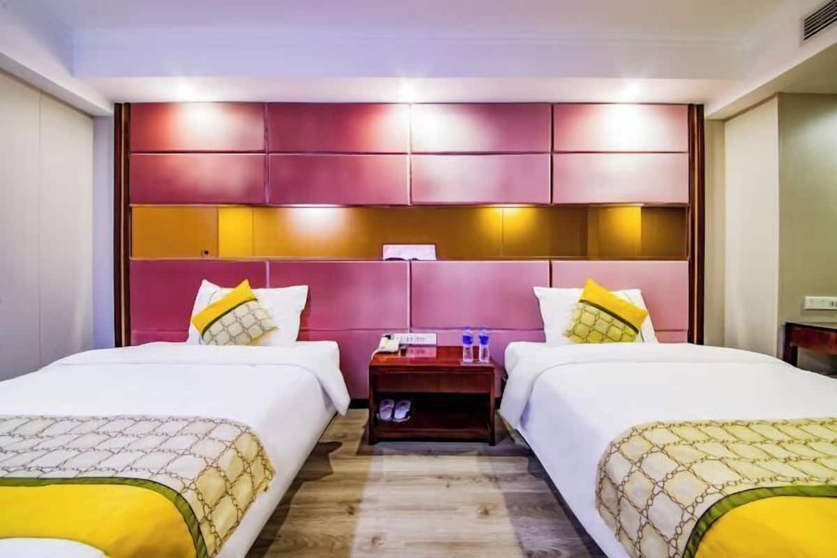 Quarto de hotel com duas camas, uma mesa de cabeceira de madeira e uma cabeceira com iluminação embutida.