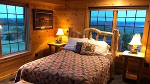 Quarto acolhedor de cabana de madeira com uma cama grande, duas luminárias de cabeceira e um banco.