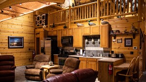 Interior acolhedor de uma cabana, com decoração em madeira, área de jantar e cozinha.