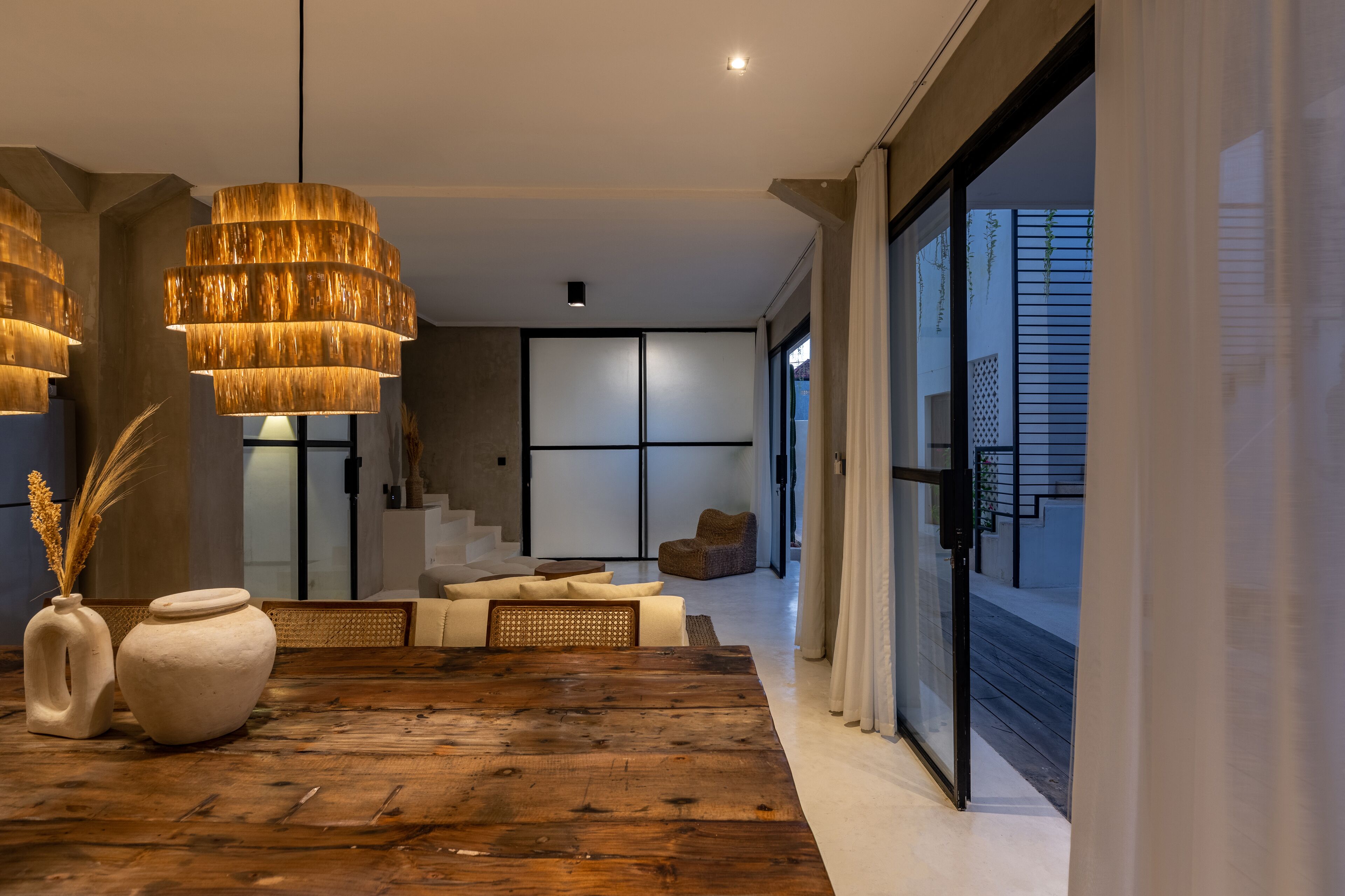 Um interior moderno com uma mesa de jantar de madeira, dois vasos de cerâmica e uma janela grande com vista para um edifício.
