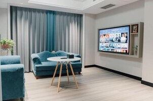 Quarto moderno com sofá azul, mesa redonda e tela grande exibindo opções de filmes.