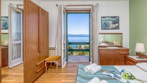 Quarto de hotel com guarda-roupa de madeira, cama com colcha listrada, mesa de cabeceira com abajur, vista para o mar e um quadro na parede.