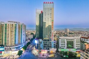Um edifício alto com fachada de vidro moderna, cercado por outros edifícios e uma rua movimentada.