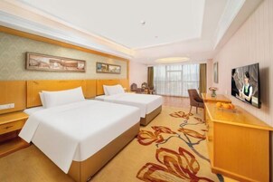 Quarto de hotel com duas camas, uma escrivaninha, uma cadeira, televisão e obras de arte nas paredes.