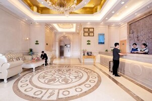 Um saguão de hotel com balcão de recepção, sofás, piso estampado e um candelabro.
