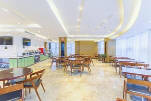 Uma ampla sala de jantar com várias mesas e cadeiras, uma cozinha equipada e uma grande janela que proporciona iluminação natural.