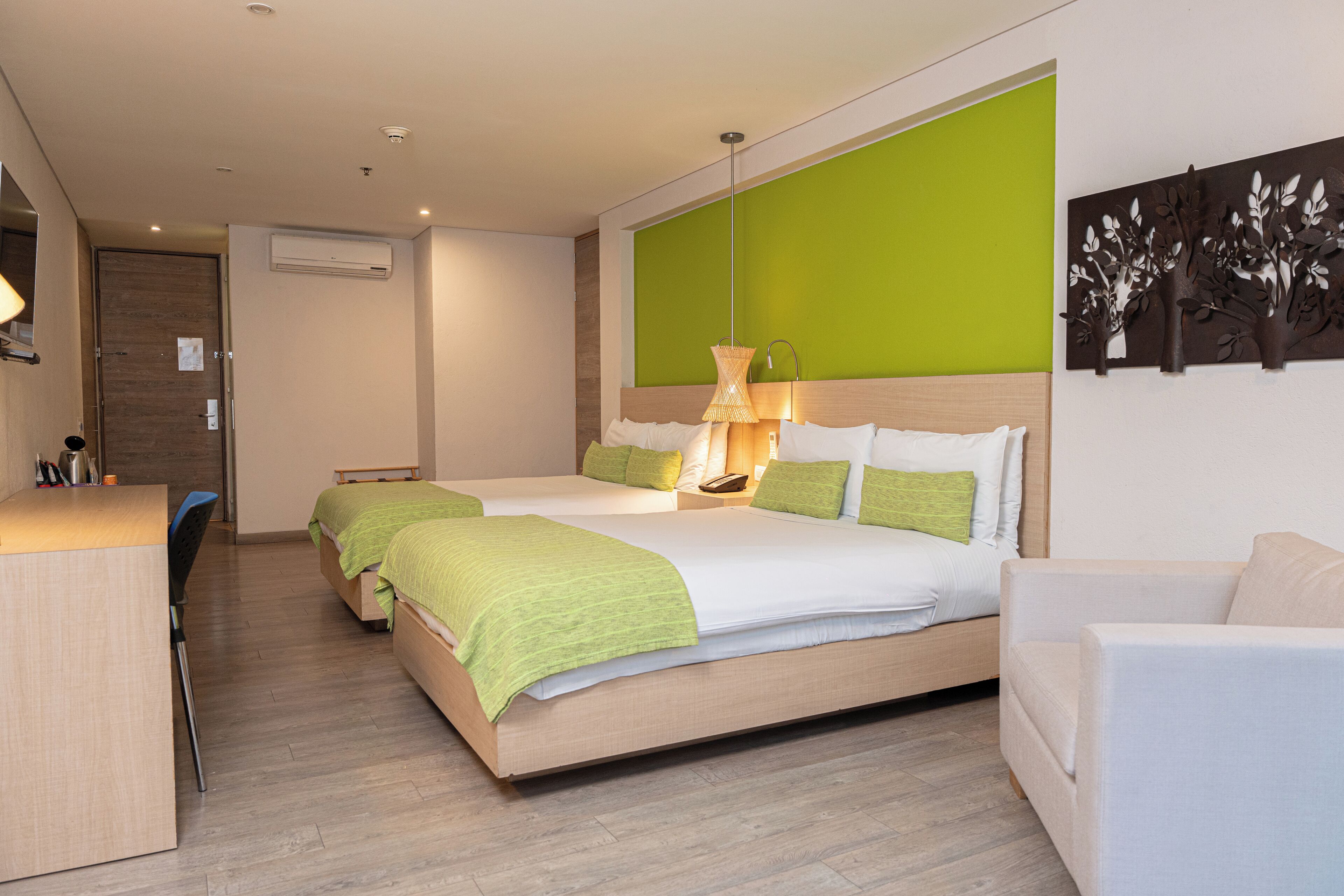 Quarto de hotel com duas camas, uma escrivaninha e uma parede verde.