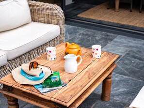 Uma mesa de madeira com um jarro branco, duas canecas com pintas, um bule amarelo, um chapéu de palha e um livro intitulado "Walks".