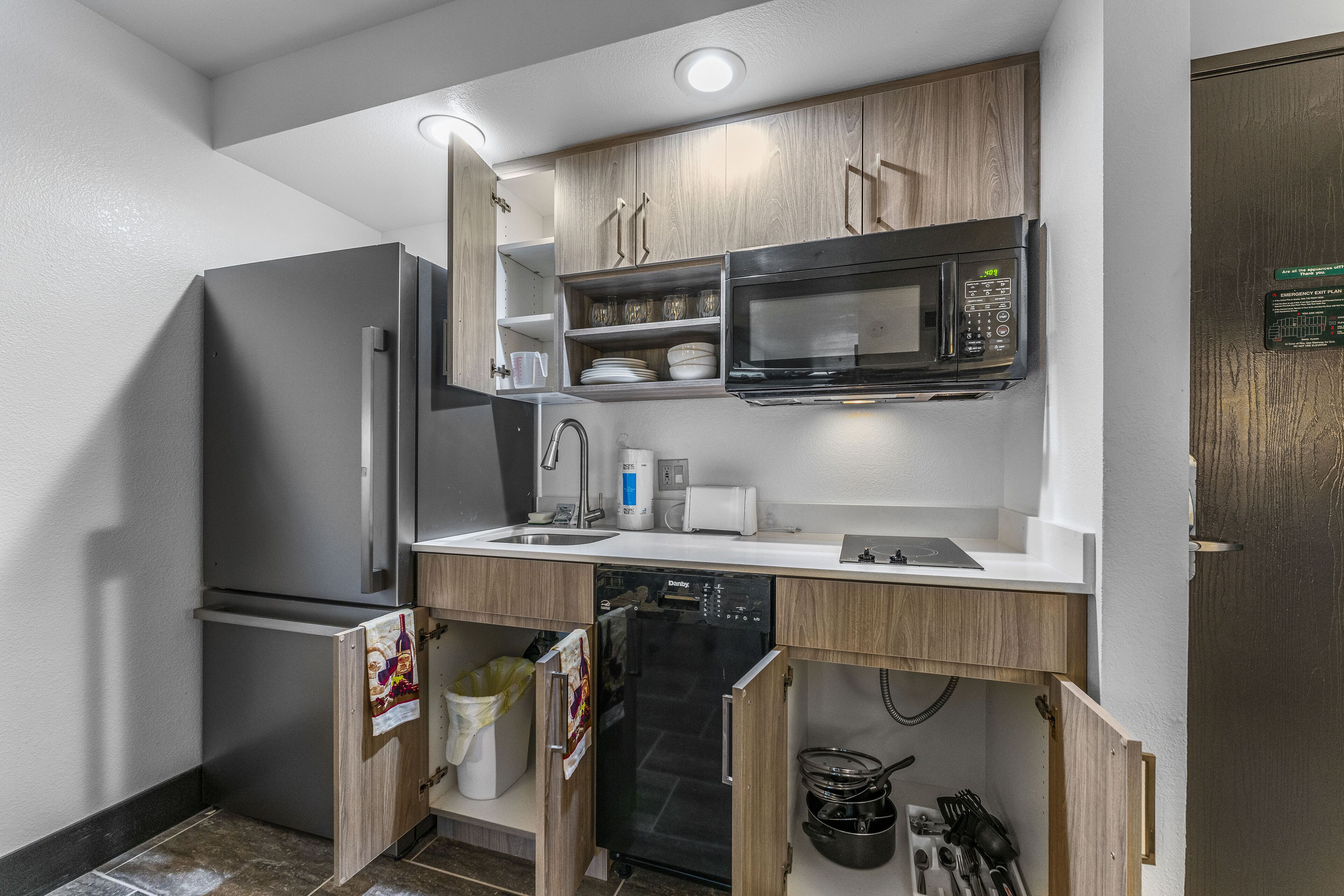 Cozinha compacta com frigorífico, micro-ondas e máquina de lavar loiça.