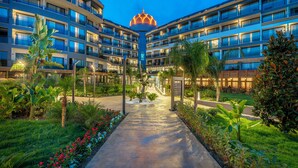 Um hotel com vários andares e uma estrutura central em forma de cúpula, rodeado por vegetação exuberante e um caminho pavimentado.