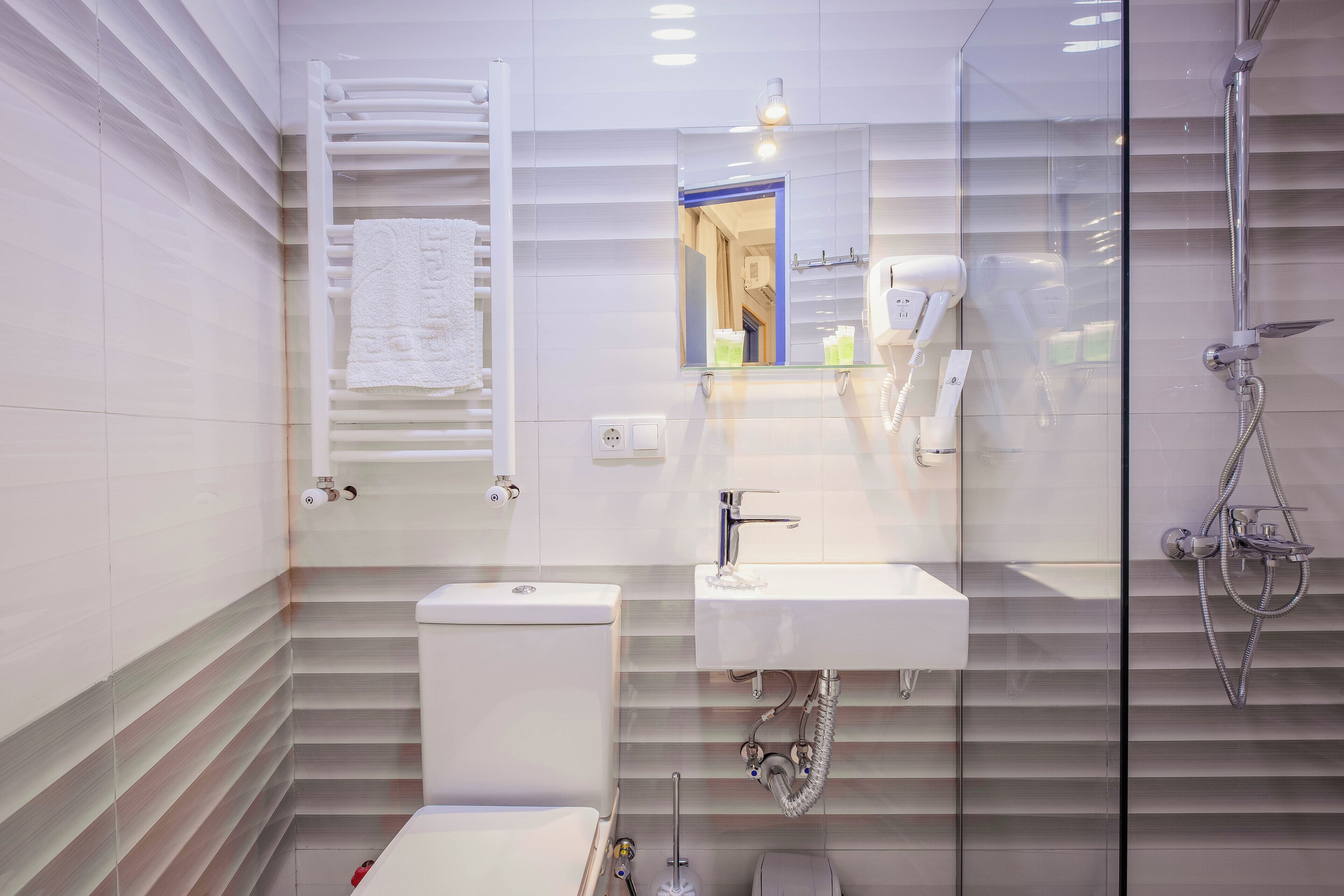 Uma casa de banho moderna com cabine de duche em vidro, lavatório branco e porta-toalhas.