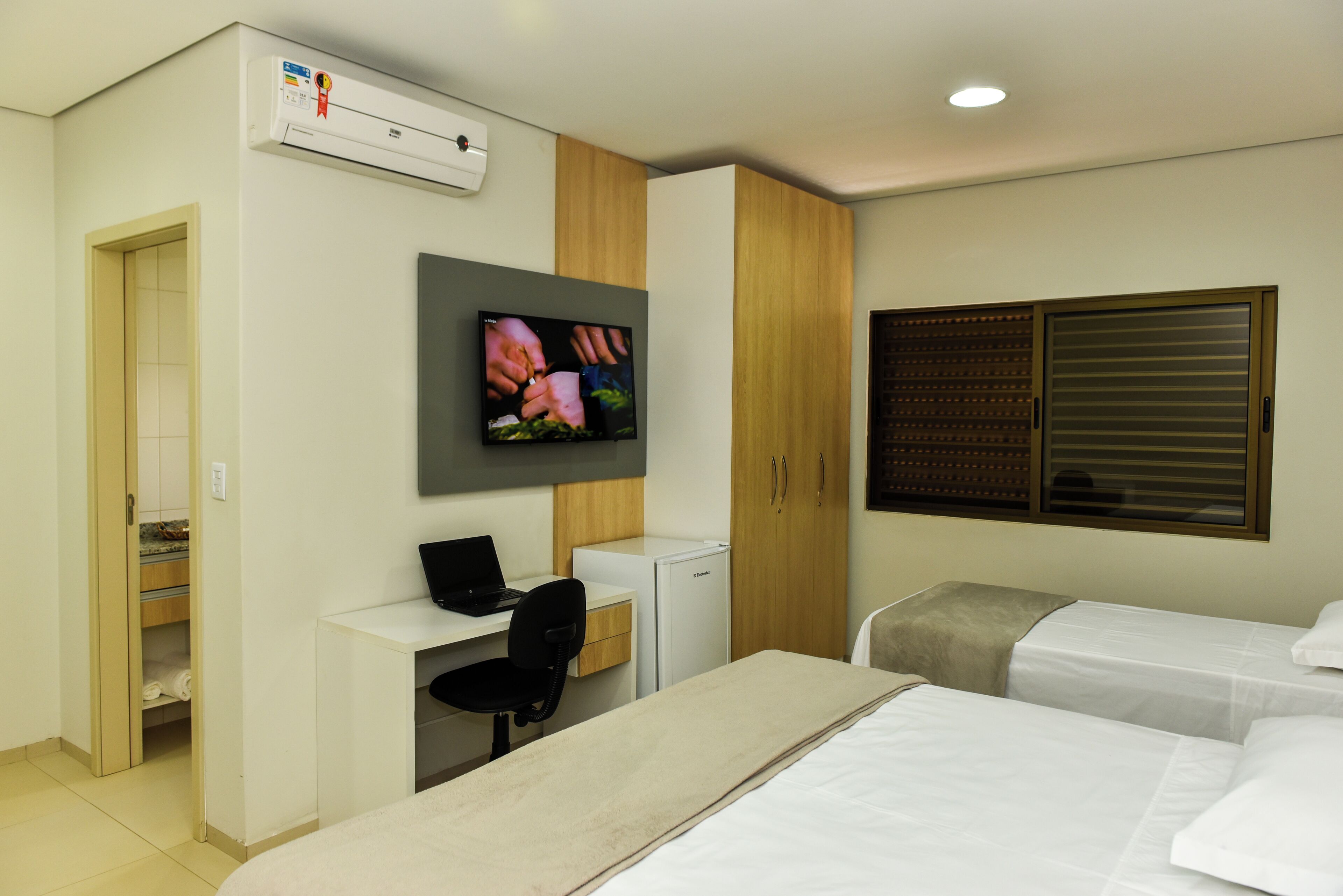Quarto de hotel com uma cama, uma escrivaninha com cadeira, uma televisão e um guarda-roupa.