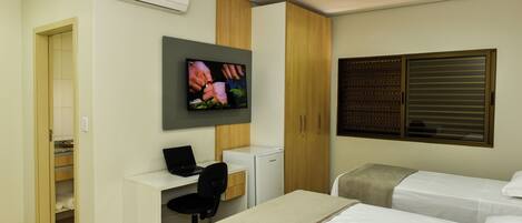 Quarto de hotel com uma cama, uma escrivaninha com cadeira, uma televisão e um guarda-roupa.