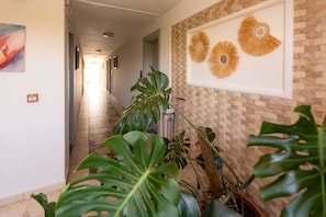 Um corredor com piso de azulejos, obras de arte emolduradas na parede e plantas em vasos.