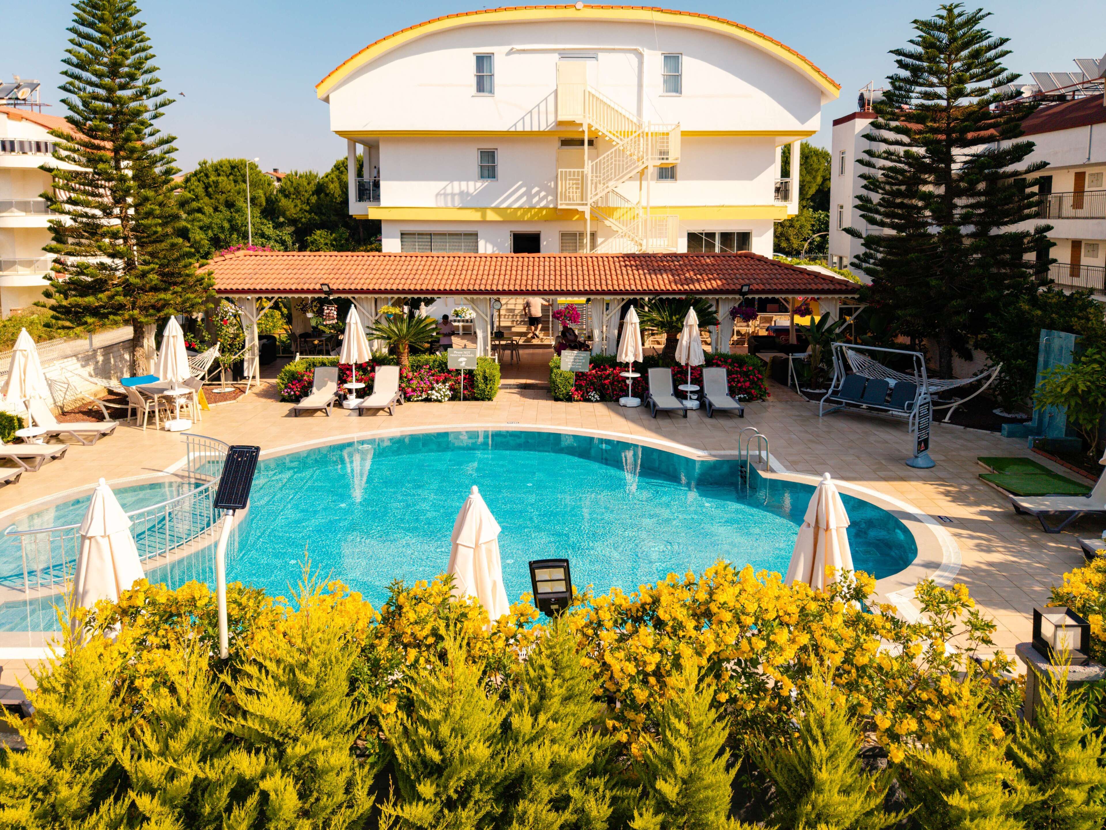 Piscina com espreguiçadeiras e guarda-sóis, rodeada por vegetação e um edifício com telhado curvo.