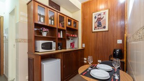 Uma cozinha compacta com armários de madeira, micro-ondas, geladeira e uma mesa de jantar posta para dois, com pratos, talheres e copos.