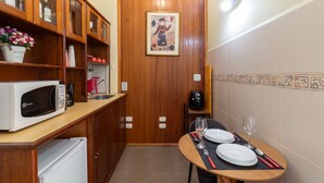 Uma cozinha compacta com armários de madeira, micro-ondas, cafeteira e mesa de jantar posta para dois, com pratos e copos.