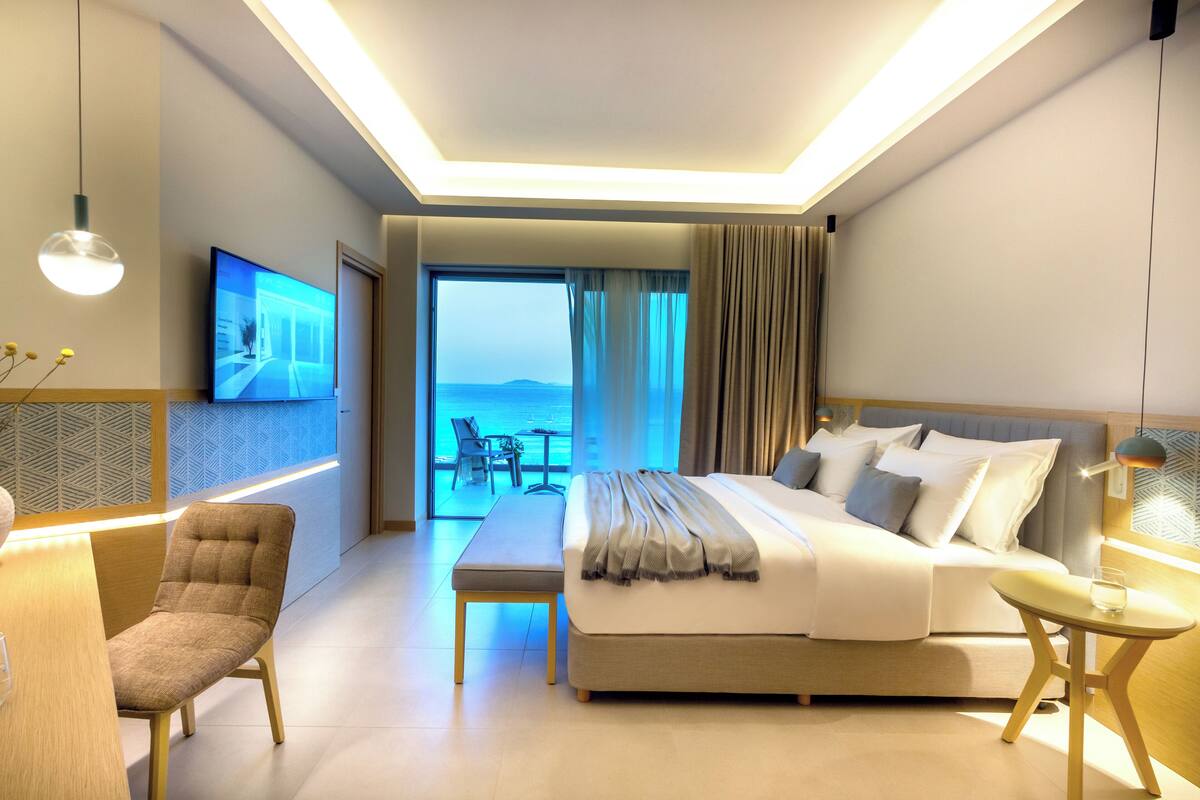 Quarto de hotel moderno com uma cama grande, escrivaninha, cadeira, televisão e varanda com vista.