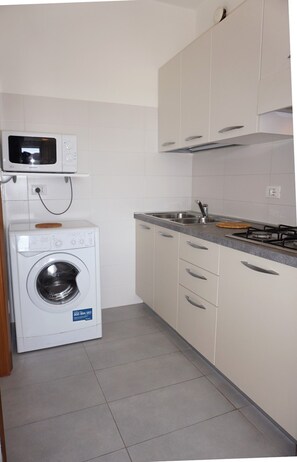Cozinha compacta com máquina de lavar, micro-ondas e fogão a gás.