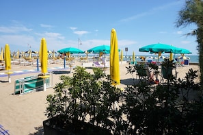Uma praia com fileiras de espreguiçadeiras e guarda-sóis, alguns com toldos amarelos e outros com toldos verdes.