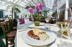 Restaurante com teto de vidro, toalhas de mesa brancas e guardanapos roxos.