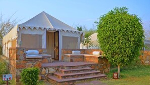 Alojamento tipo tenda com fachada de pedra, um pequeno alpendre com degraus e um arbusto bem aparado.