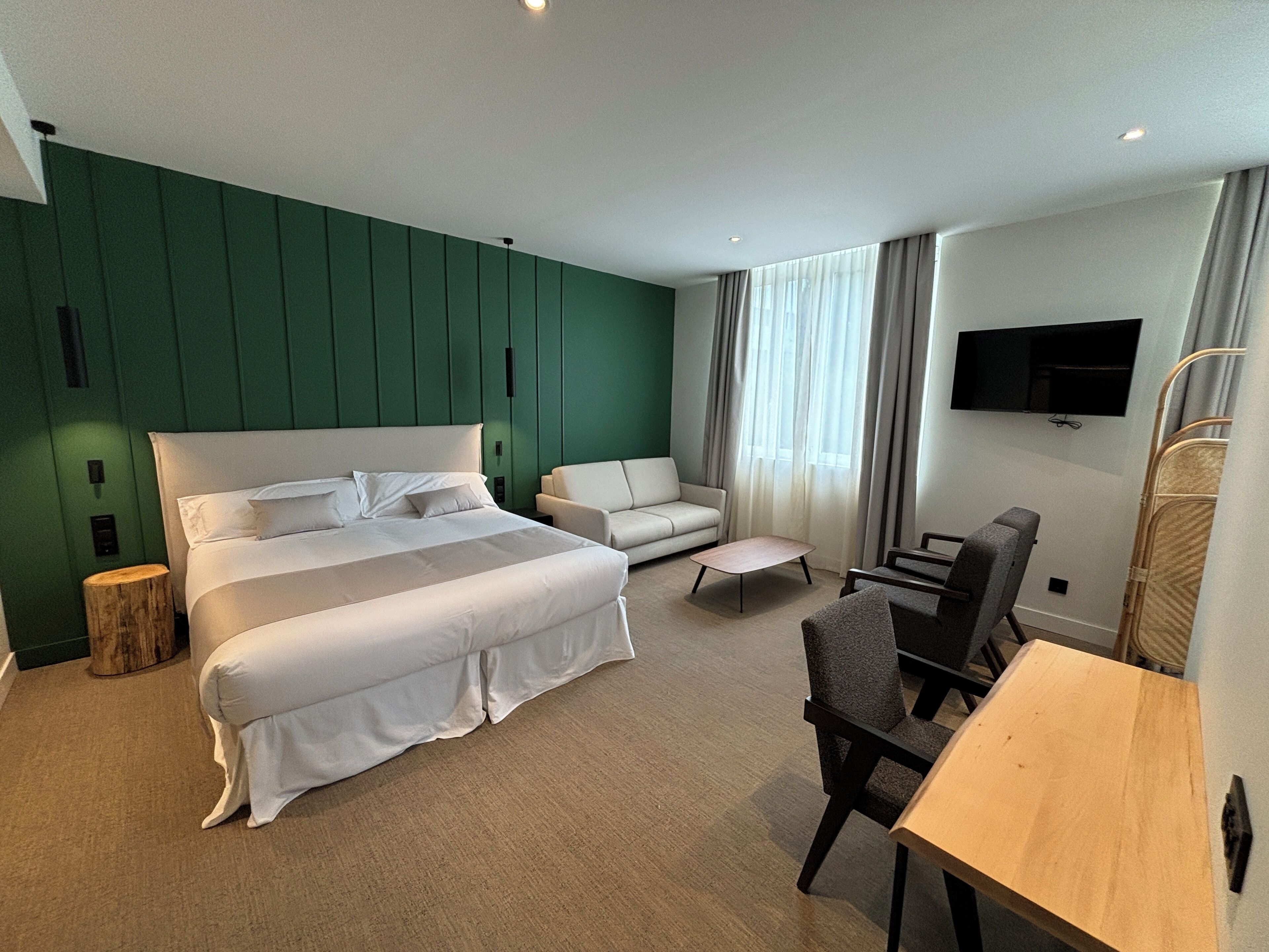Quarto de hotel moderno com uma cama grande, um sofá, uma escrivaninha e uma televisão fixada na parede.