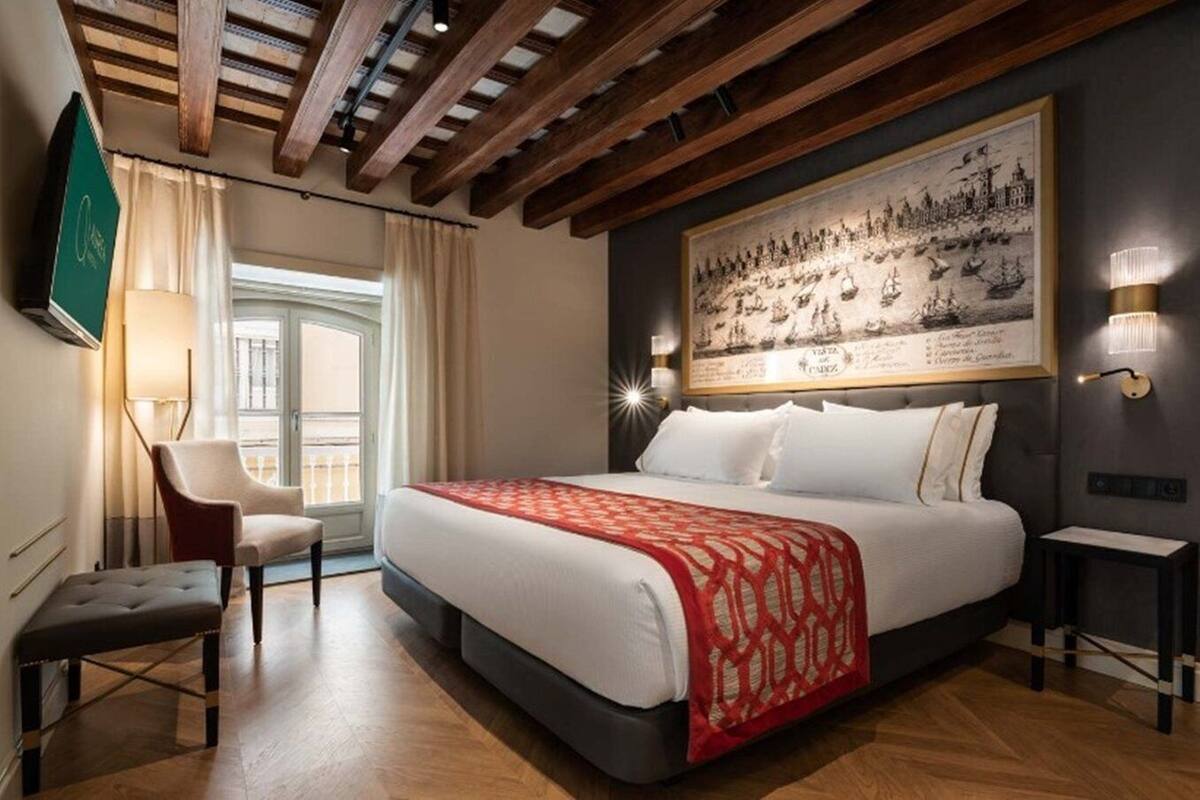 Quarto de hotel com uma cama grande, uma cadeira, uma escrivaninha e um quadro na parede.