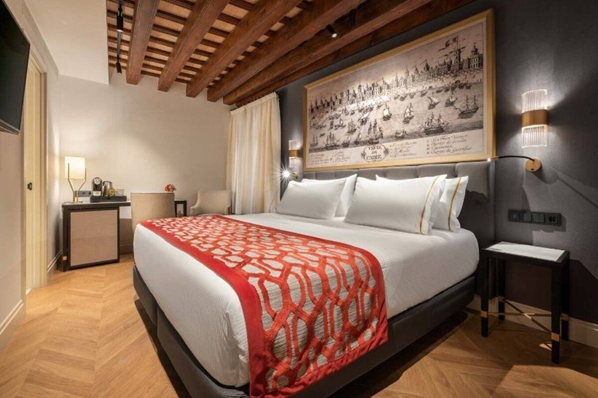 Quarto de hotel moderno com uma cama grande, vigas de madeira no teto e um mapa grande emoldurado na parede, além de uma pequena mesa com uma luminária.