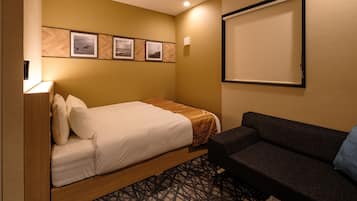 Quarto de hotel com uma cama, um sofá, uma tela de projetor fixada na parede e uma série de quadros pendurados.