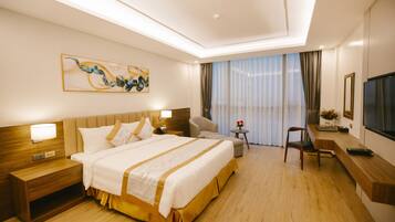 Quarto de hotel com uma cama grande, mesas de cabeceira, escrivaninha, cadeira, televisão e janela com cortinas.