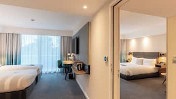 Quarto de hotel com duas camas, uma escrivaninha, uma cadeira, uma televisão e uma mesa de cabeceira com luminária.