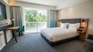 Quarto de hotel com uma cama grande, uma mesa com cadeira, televisão e varanda com cortinas.