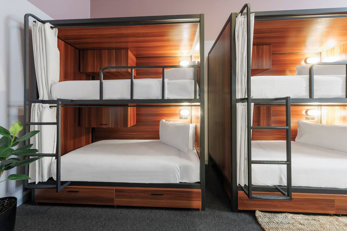 Quarto com beliches, cabeceiras de madeira, roupa de cama branca e abajures.