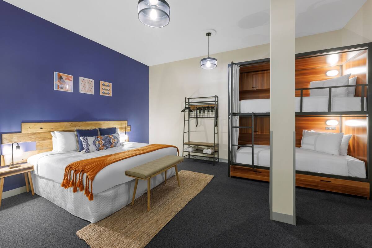 Quarto de hotel moderno com uma cama grande, um banco, um guarda-roupa e uma pequena escrivaninha.