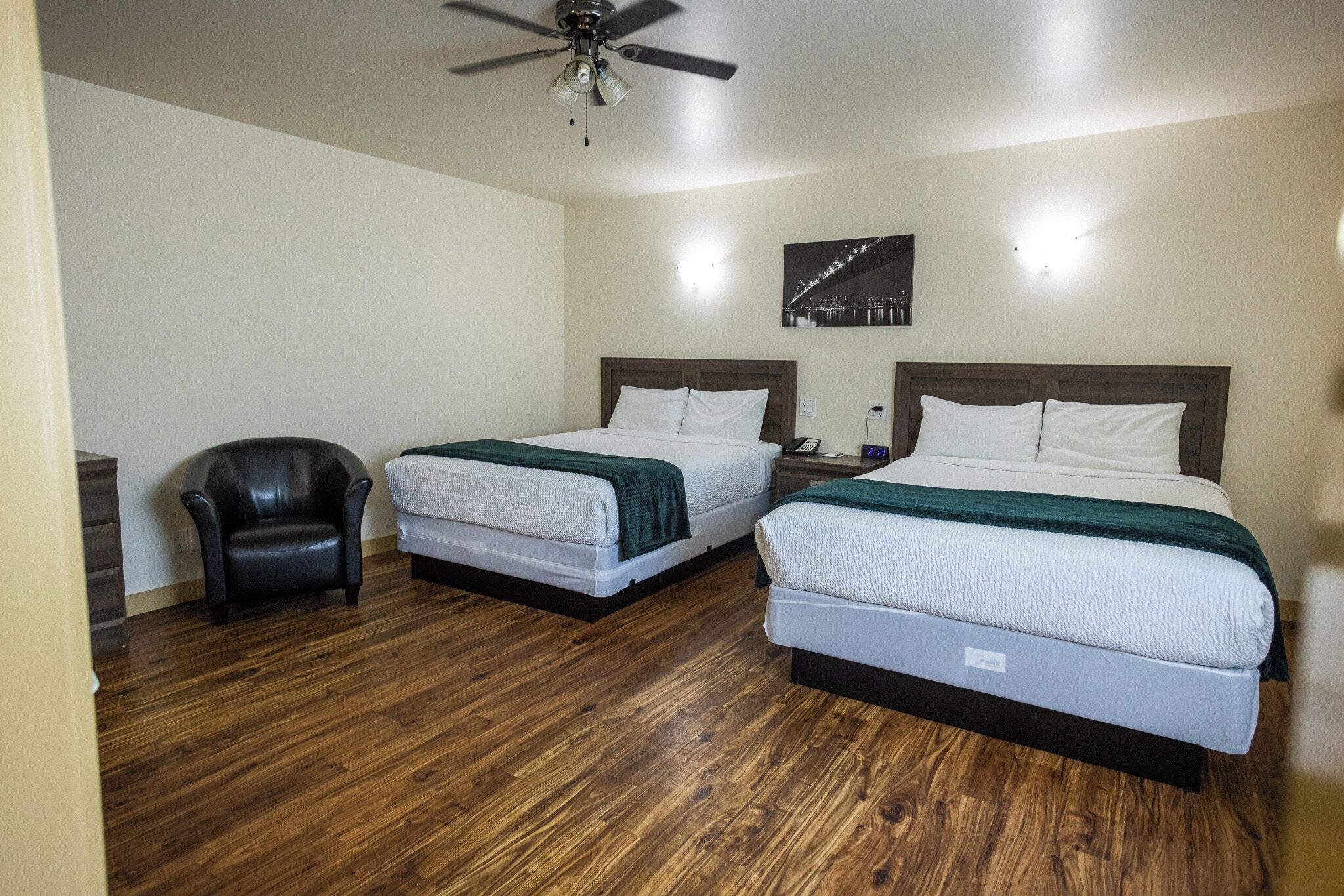 Quarto de hotel com duas camas, uma cadeira, um ventilador de teto e uma luminária na parede.