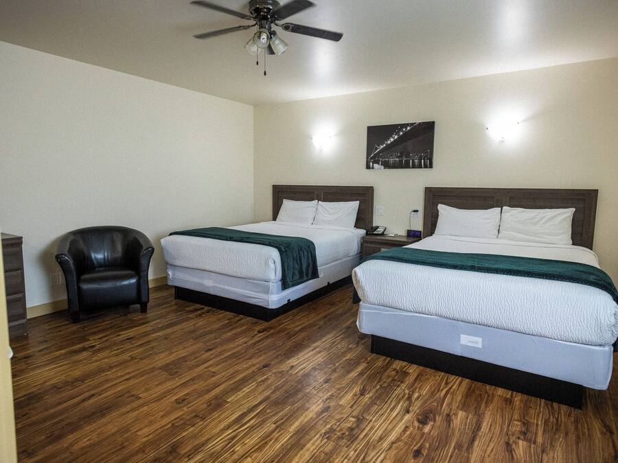 Quarto de hotel com duas camas, uma cadeira, um ventilador de teto e uma luminária na parede.