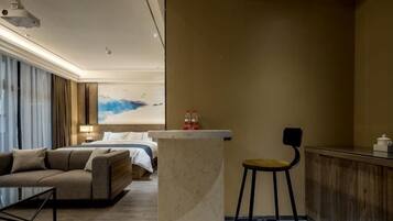 Quarto de hotel com cama, área de estar, bar e uma pintura grande na parede.