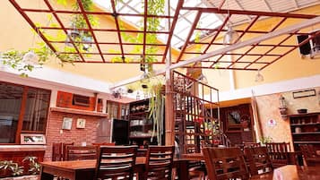 Um espaço de refeições interno com mesas e cadeiras de madeira, uma parede de tijolos com quadros emoldurados e um teto com padrão quadriculado.