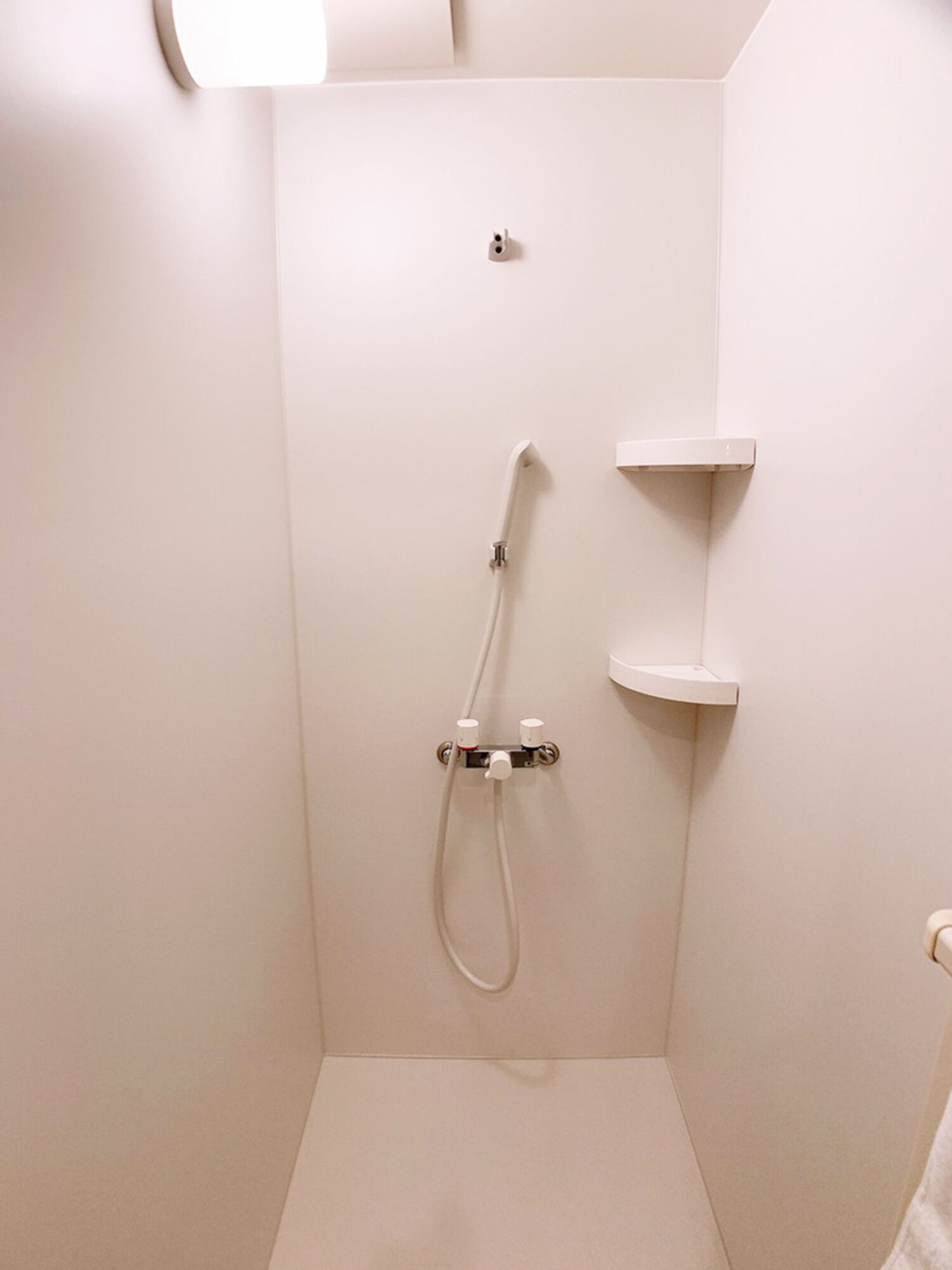 Um chuveiro pequeno e branco, fechado, com um chuveiro manual e controle na parede.