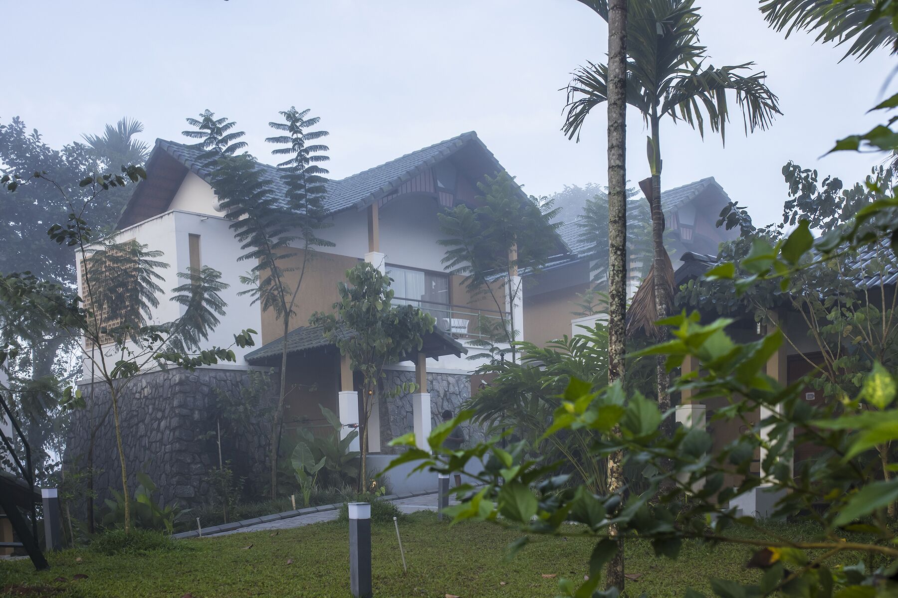 Um edifício de vários andares com design moderno, rodeado por vegetação exuberante e palmeiras.