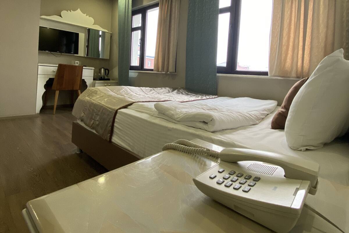 Quarto de hotel com cama, escrivaninha, cadeira, televisão e telefone.