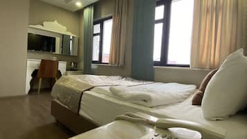 Quarto de hotel com cama, escrivaninha, cadeira, televisão e telefone.