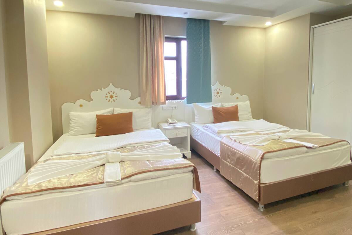 Quarto de hotel com duas camas, uma janela com cortinas, mesa de cabeceira e guarda-roupa.