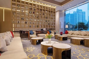 Um hall de hotel moderno com uma grande estante de livros, assentos confortáveis e vista para a cidade.