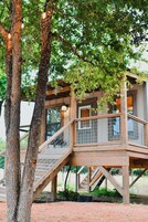 Uma cabana de madeira em uma árvore, com escada e guarda-corpo de metal.
