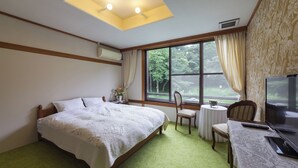 Quarto com cama, escrivaninha, cadeira, televisão e janela com cortinas.